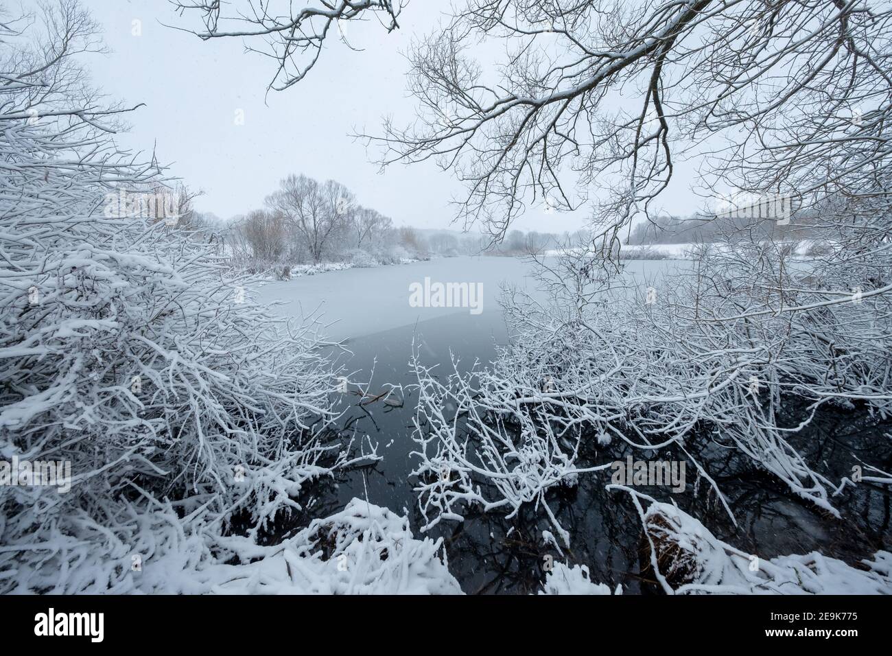 snowy winter landscape in a calm and quiet mood with a lake framed by ...