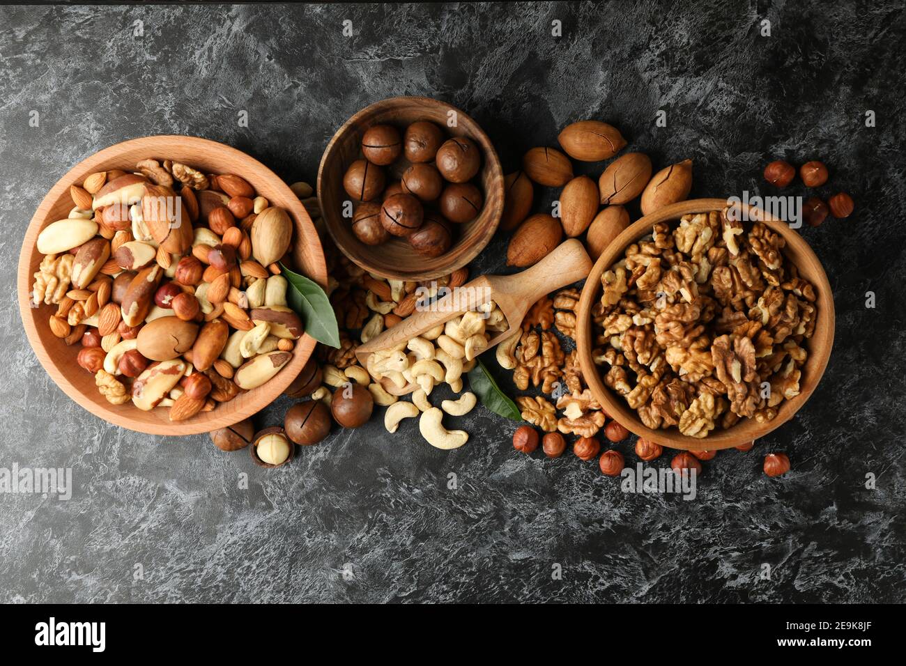 Bowl and wooden scoop with different nuts on black smokey background ...