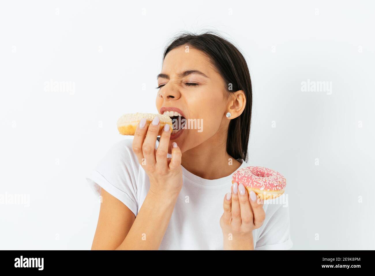Portrait hungry young woman craving eating donuts isolated over white ...