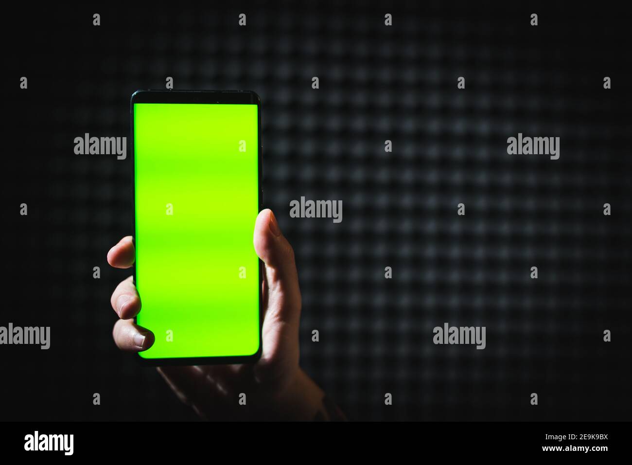 Black mobile phone with a green screen, isolated on a blurry dark ...