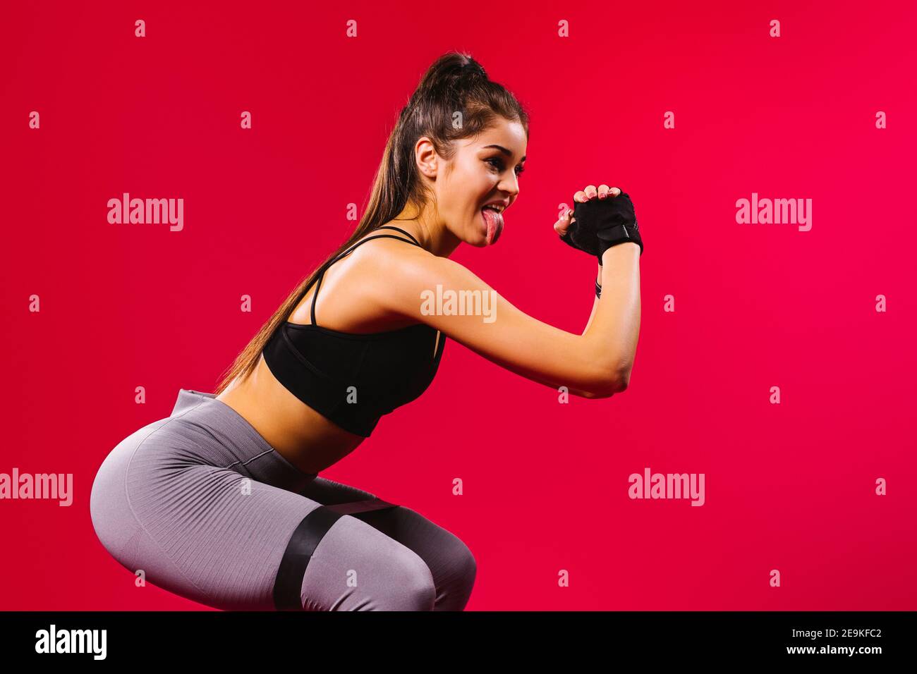 A girl with a pumped-up figure squats with a resistance elastic band ...