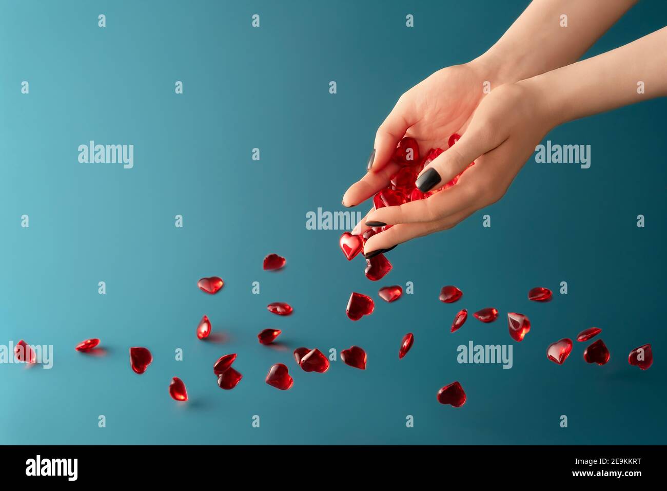 Beautiful card with female hands pouring red hearts on dark aqua ...