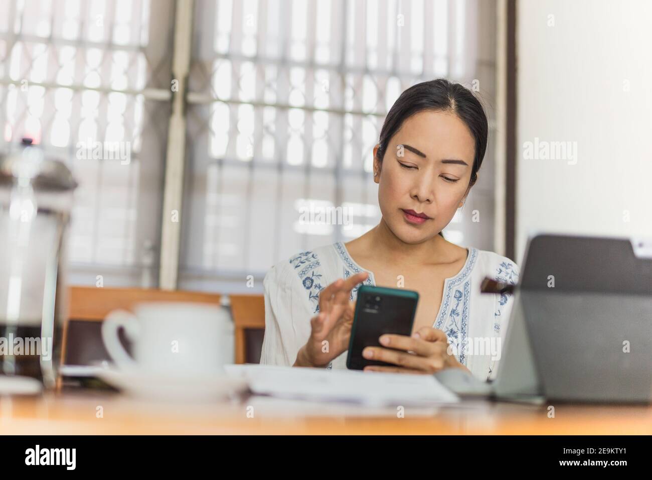Businesswoman using mobile phone while working on laptop at home Stock ...