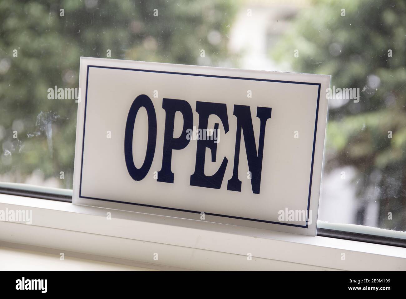 White sign with open written on it with blurred trees on the backgro ...