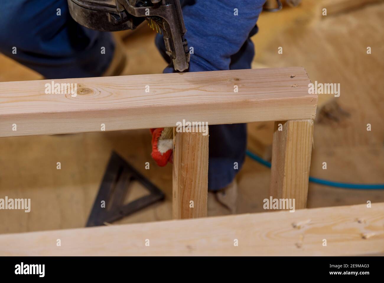 Workmen using pneumatic nail gun install wood framing beams on new home ...