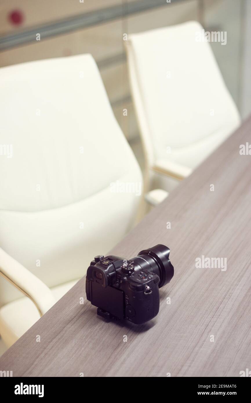 Photographic camera on an office table with some white seats on the ...