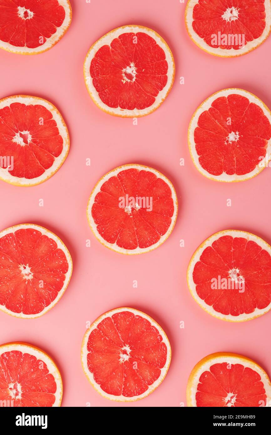 Patterns of slices of juicy grapefruit on a pink background, a ...