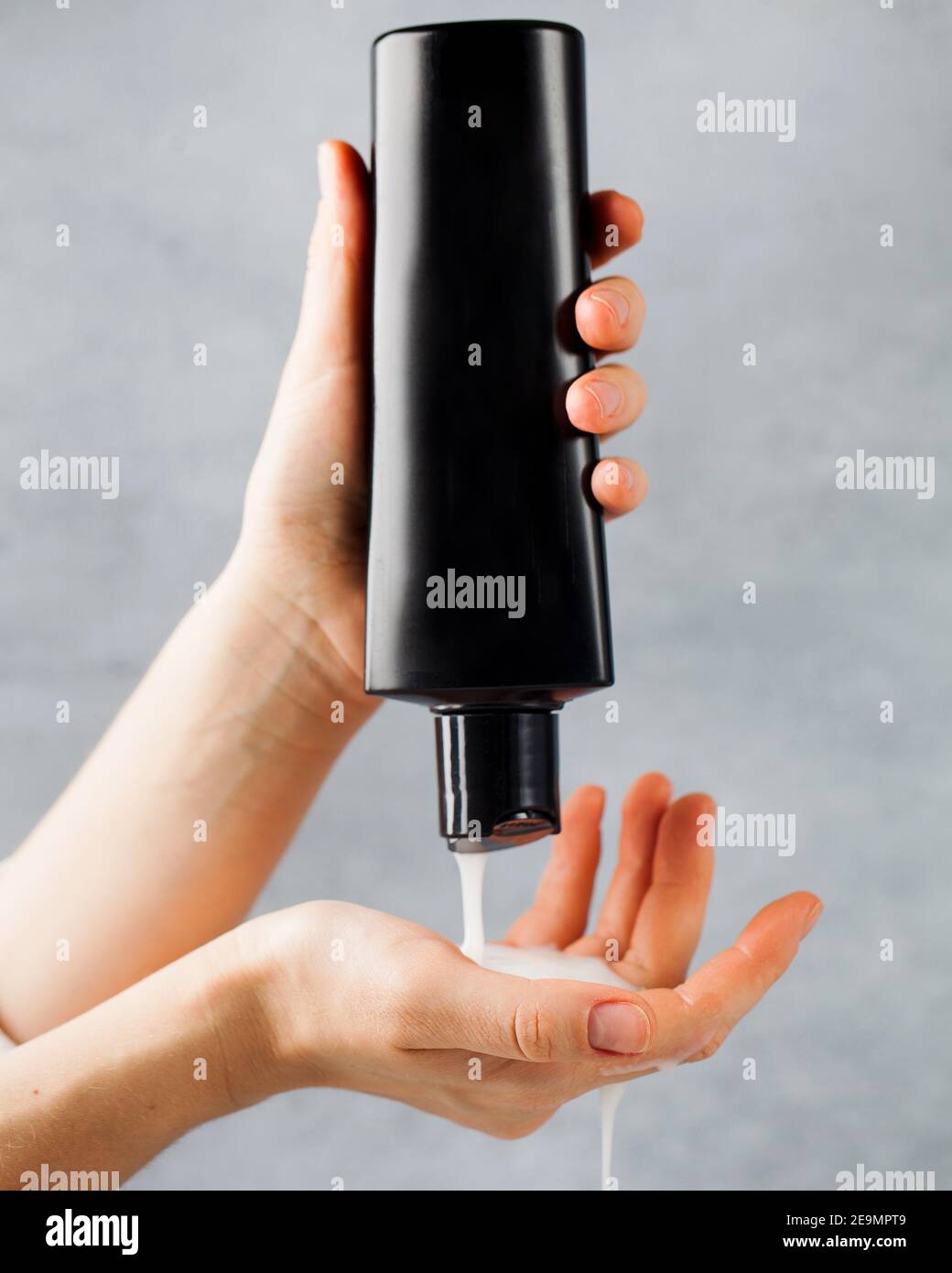 Shampoo, hair rinse is poured from a black tube into a woman's hand. An ...
