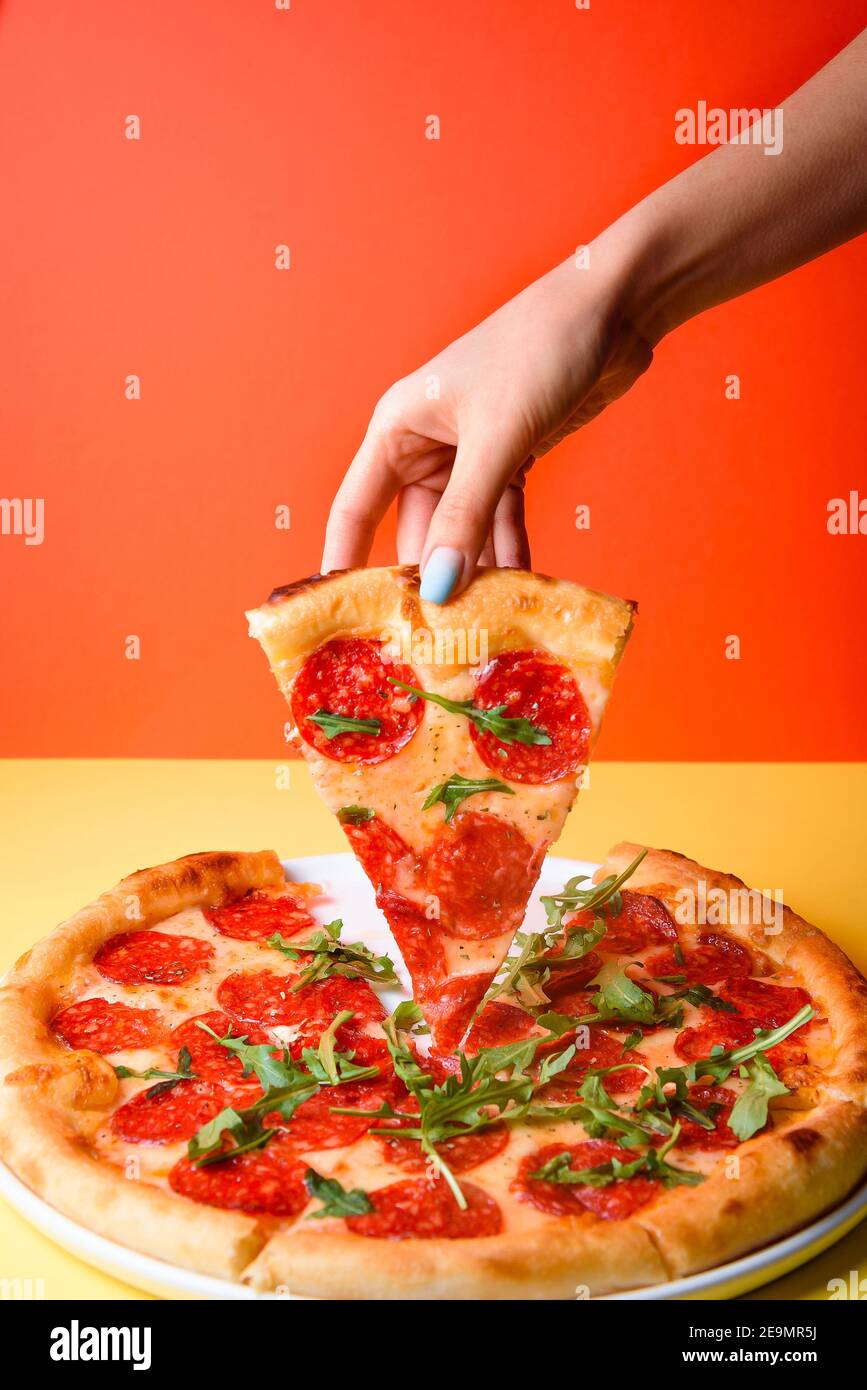 hand holds pizza, tearing off a slice on a colored background pepperoni ...
