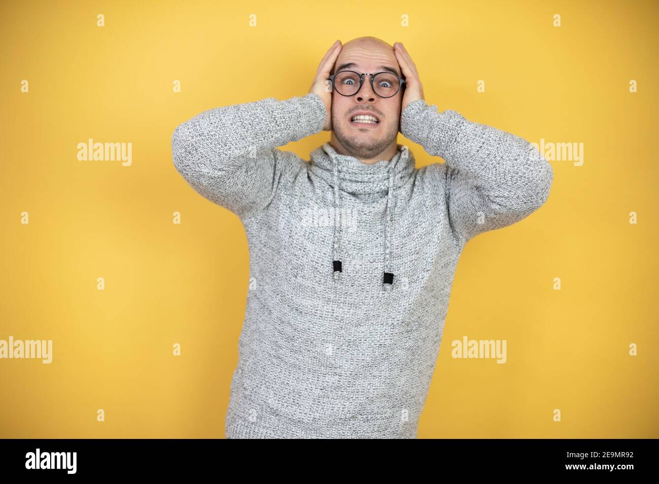 Young bald man wearing glasses over yellow background crazy and scared ...