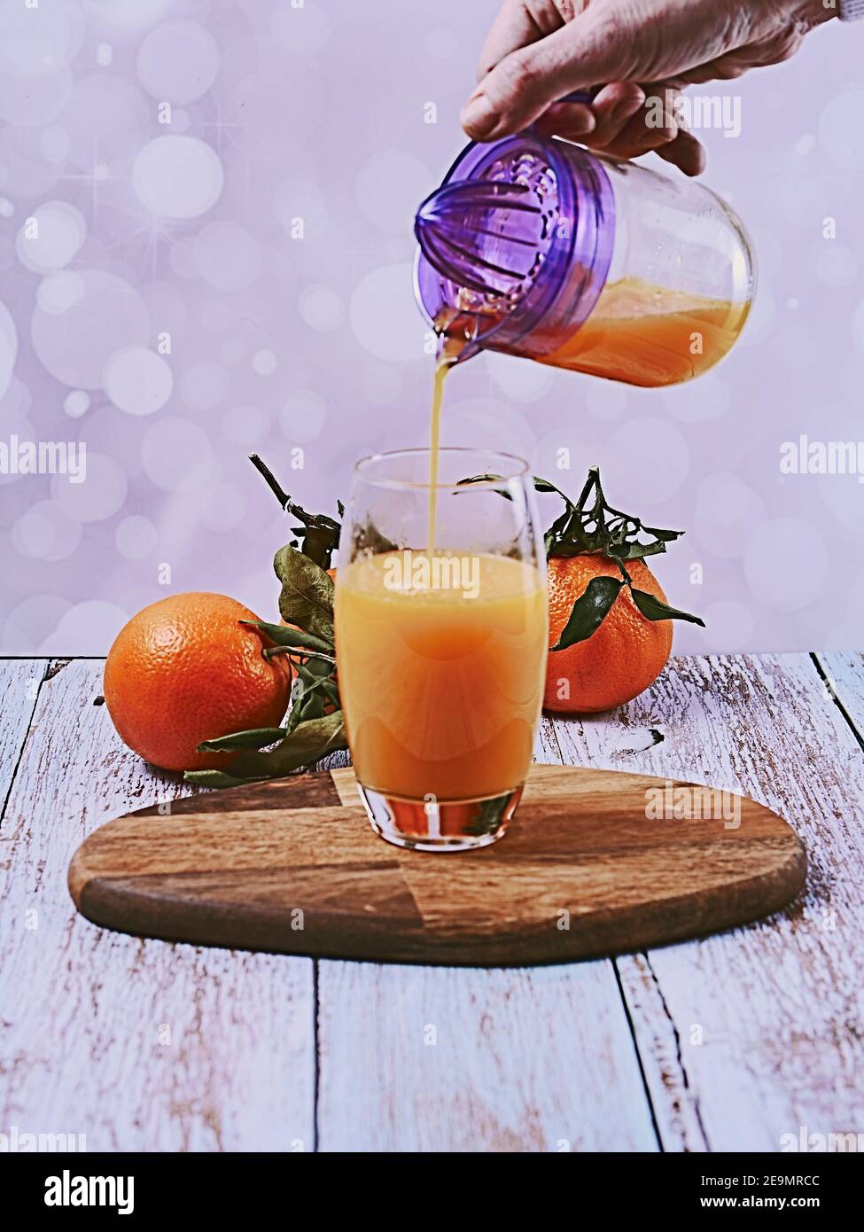 Hand pouring orange juice into glass with glass squeezer, wooden table ...