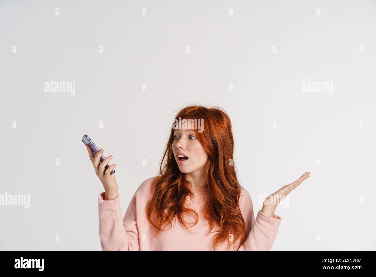 Ginger beautiful shocked girl holding cellphone and throwing up hands ...