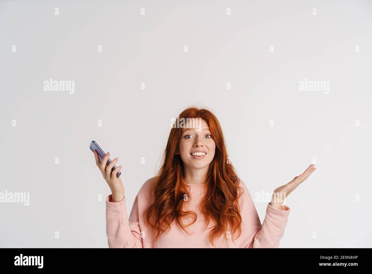 Ginger beautiful joyful girl holding cellphone and throwing up hands ...