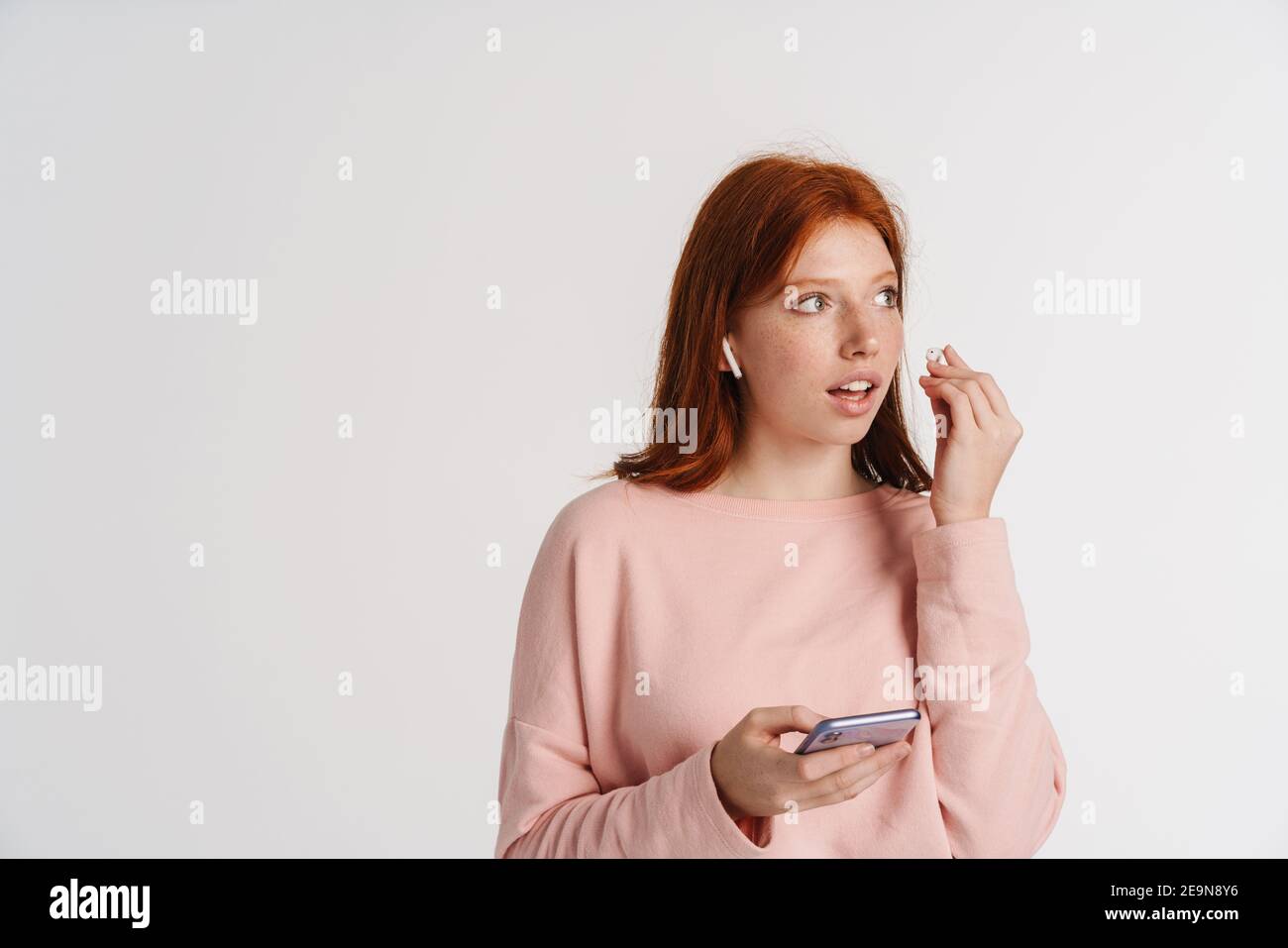 Ginger beautiful thinking girl using cellphone and wireless earphones ...