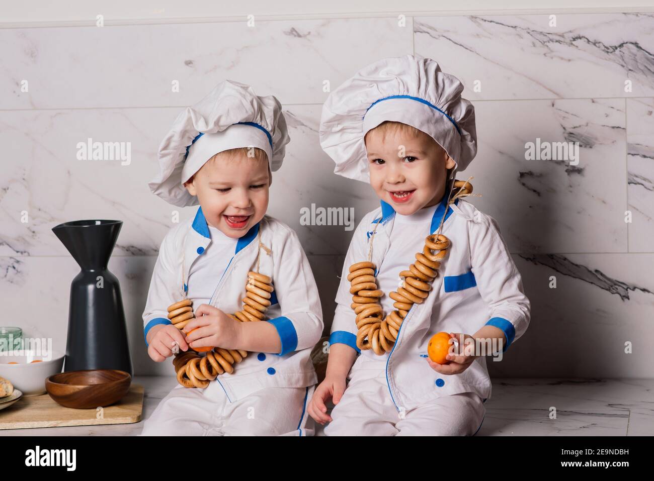 Little cute cook with cutlery sitting on kitchen, twin brothers ...