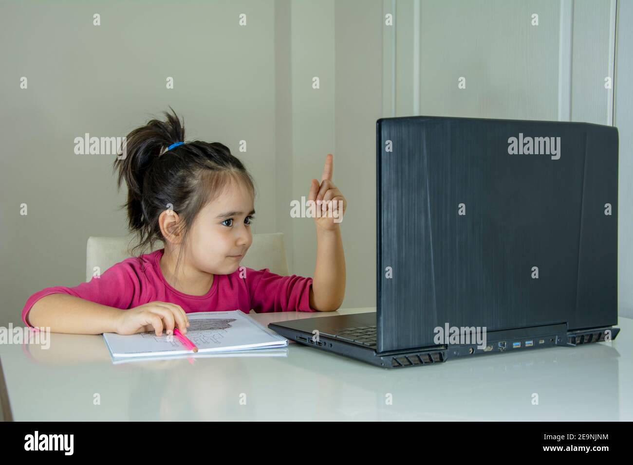 Little girl raising hands in online education Stock Photo - Alamy