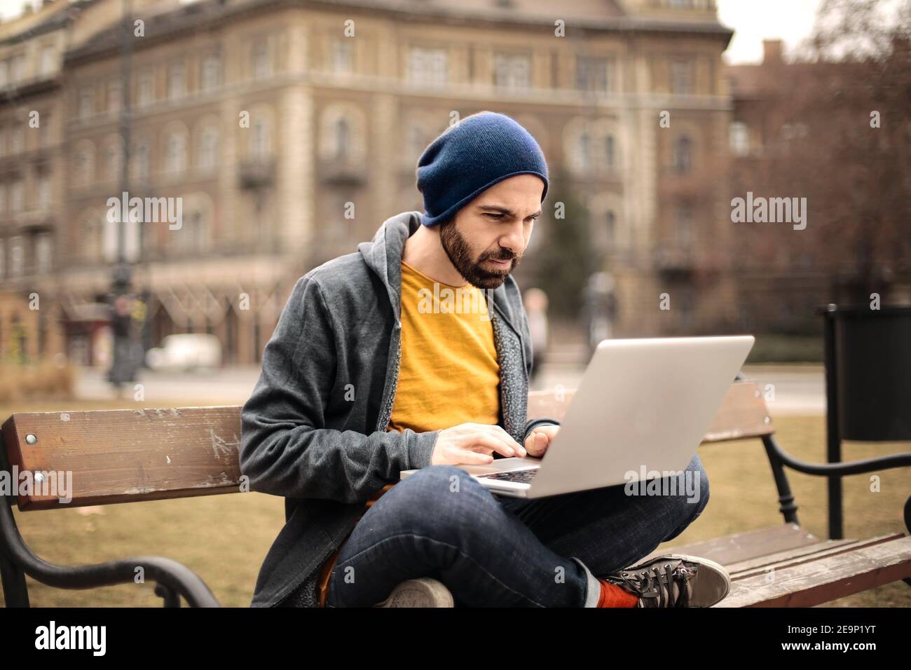 Shallow focus of a stylish young man sitting on a bench and working on ...