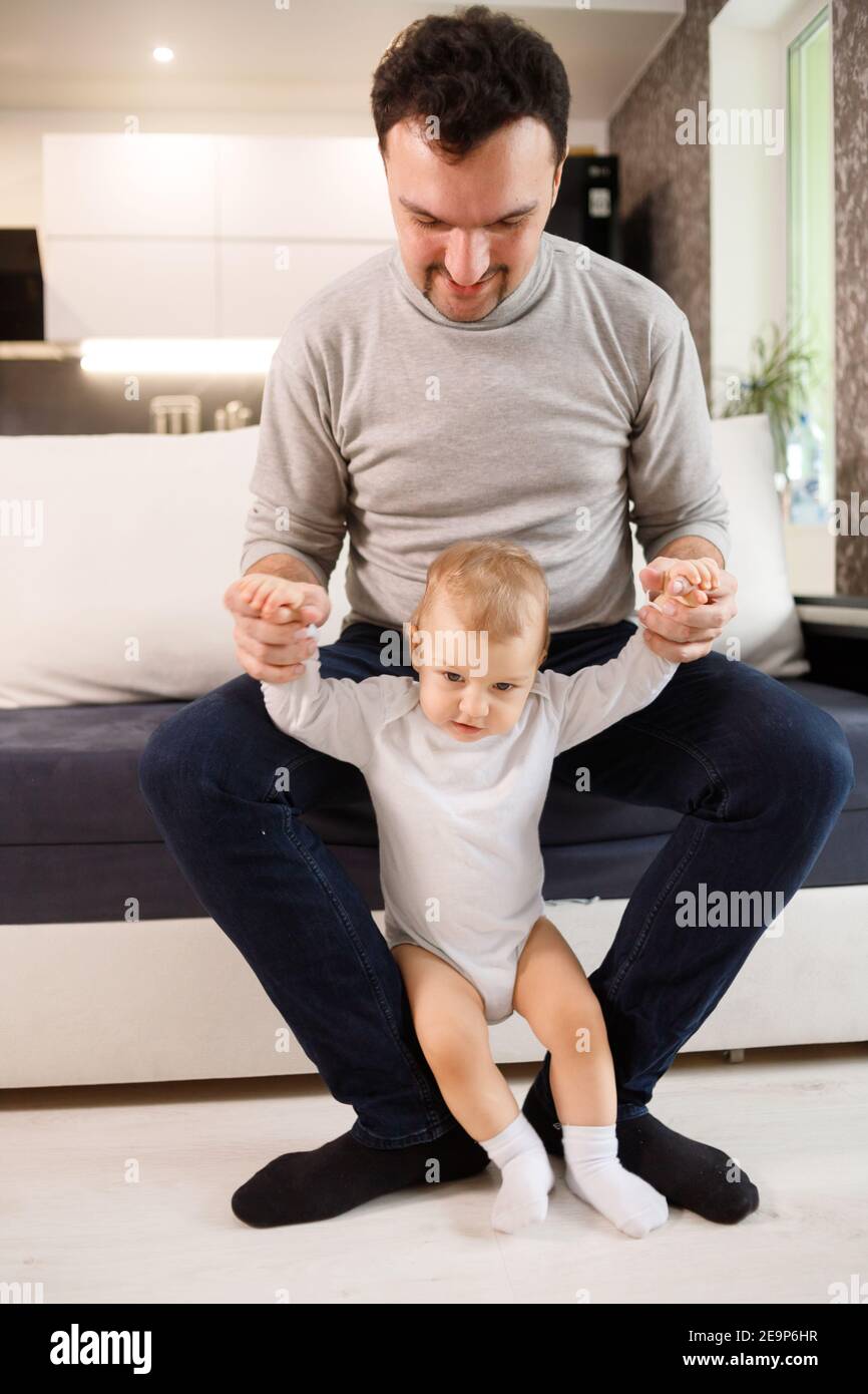 Young father assisting walking his infant son teaching to walk at home ...