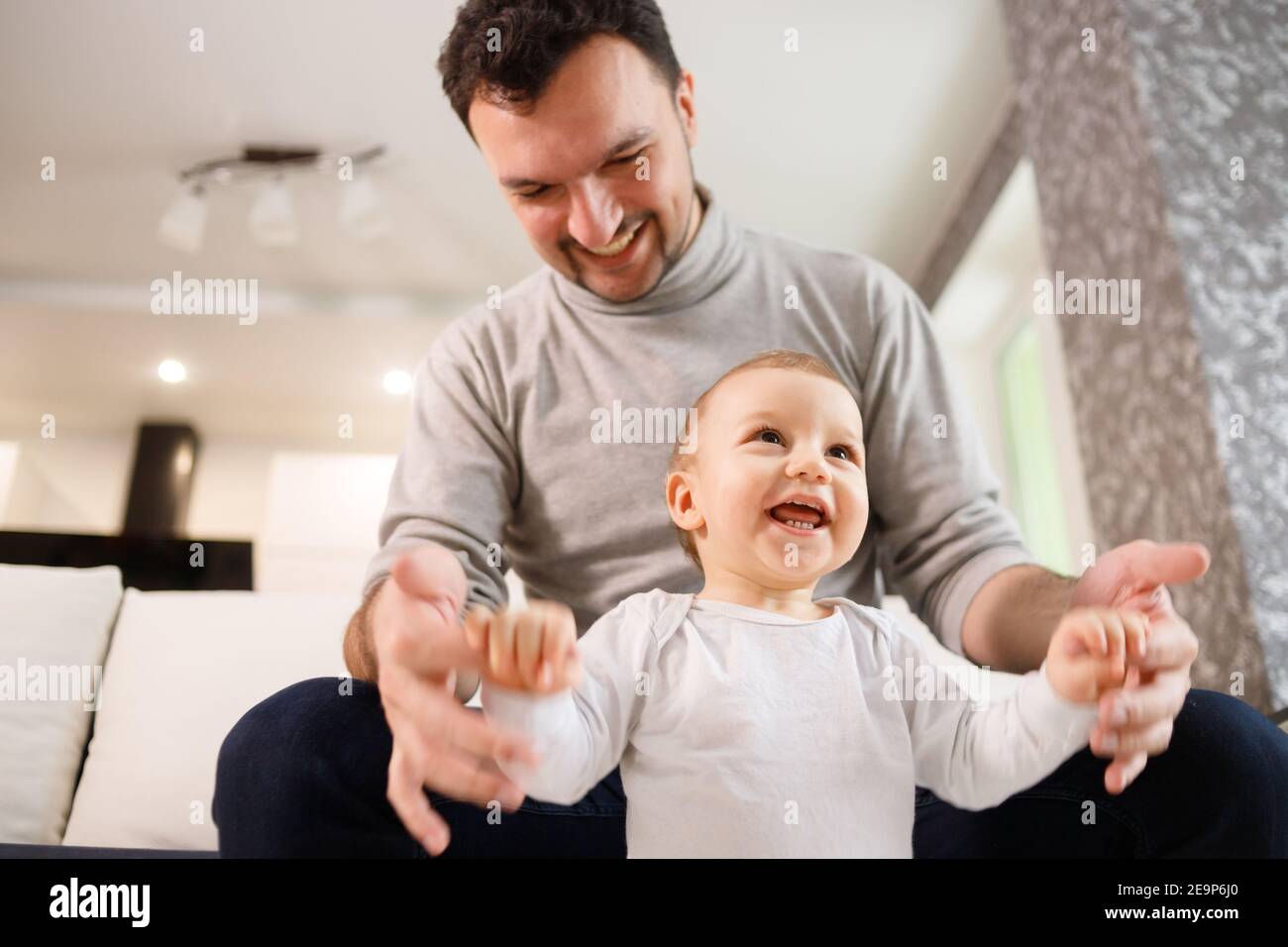 Young father assisting walking his infant son teaching to walk at home ...