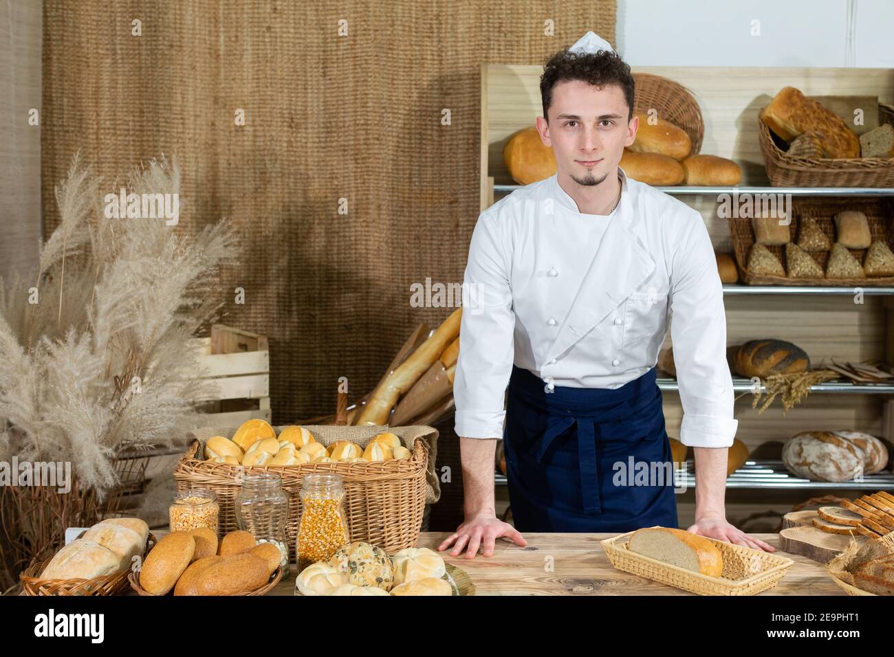 A tall and handsome baker in a baker's outfit stands behind the counter ...