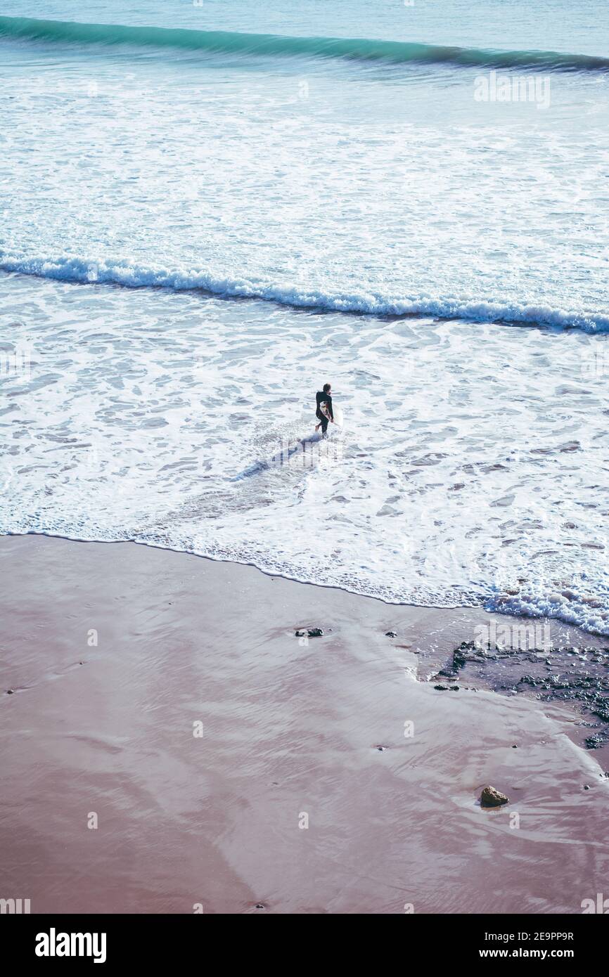 Surfer boy entering the sea with waves in the background, from above ...
