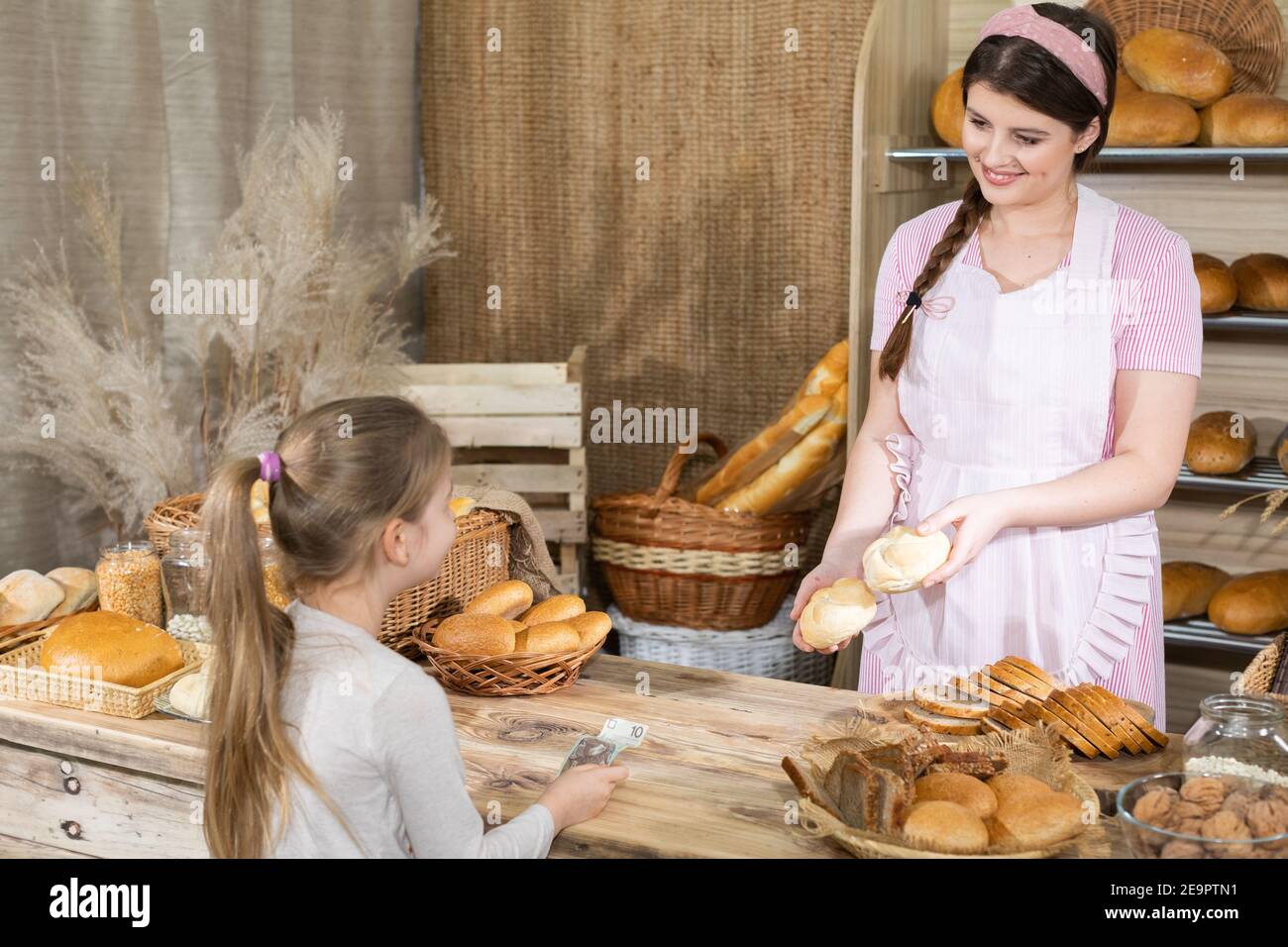 A little girl waits in front of the counter in a bakery store until an ...