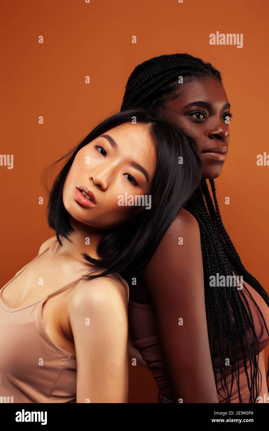 young pretty asian and afro woman posing cheerful together on brown ...