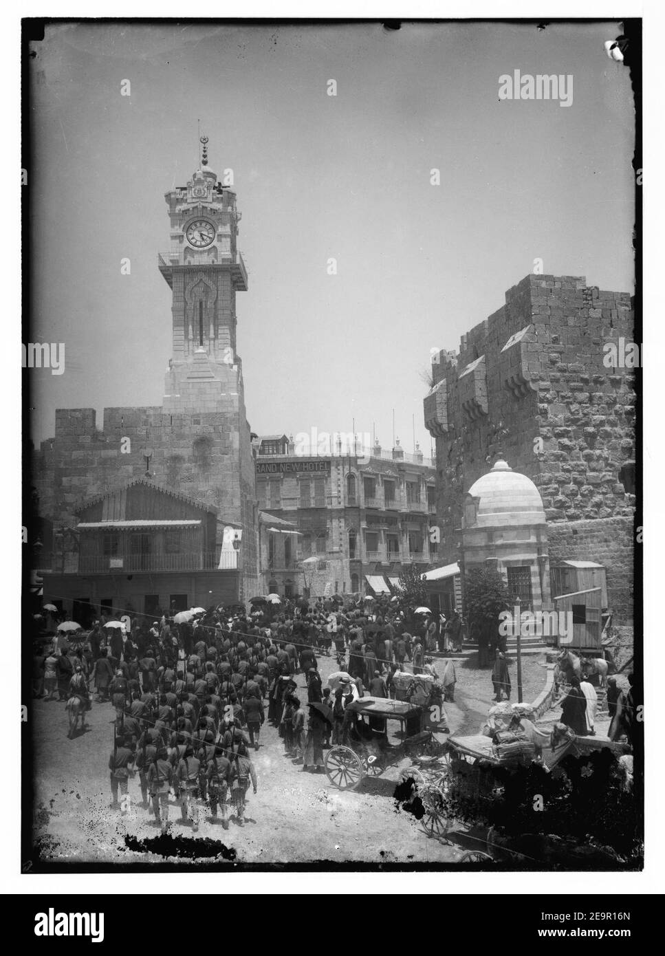 Marching in front of Am. (i.e., American) Colony store. Grand New Hotel ...