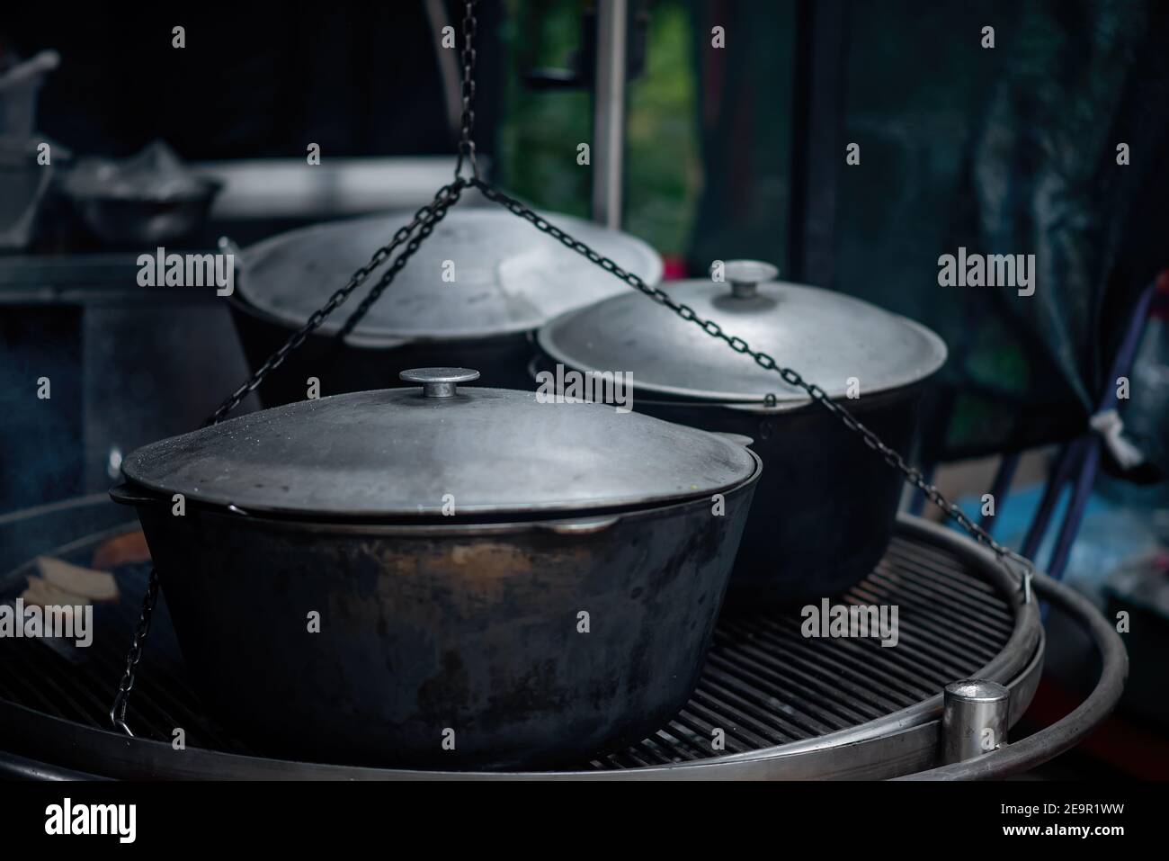 Large gray iron aluminum cauldrons on the grill, in which a campfire is ...