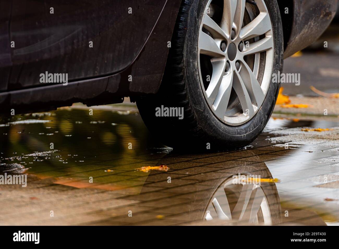 puddle on the pavement with a reflection of the car wheel and colorful ...