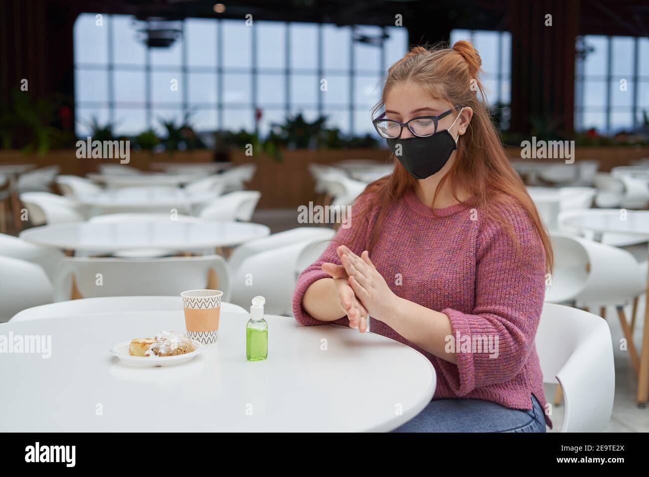 Young woman in protective mask applies sanitizer before lunch at fast ...