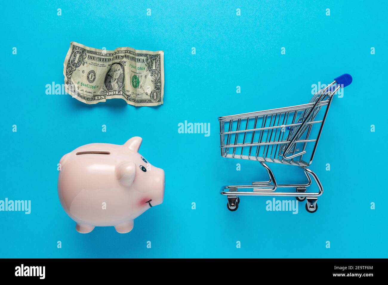Piggy bank with a crumpled dollar bancnote and shopping cart on blue ...