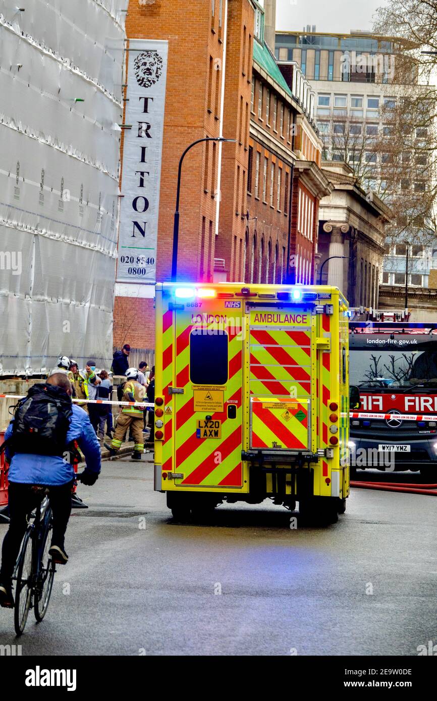 A cyclist looks up at a fire as the road is blocked by ambulances and ...
