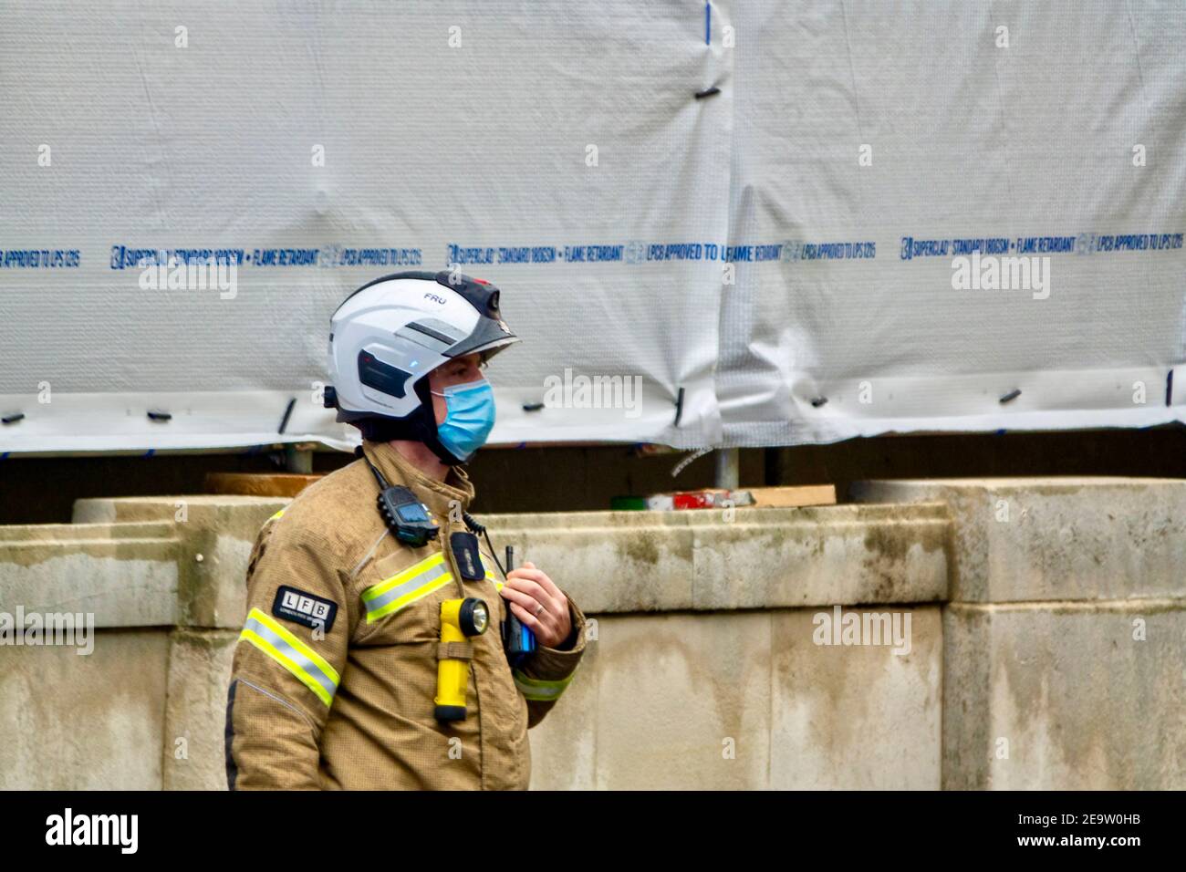 A London Fire Brigade firefighter commander, wearing a face mask, using ...