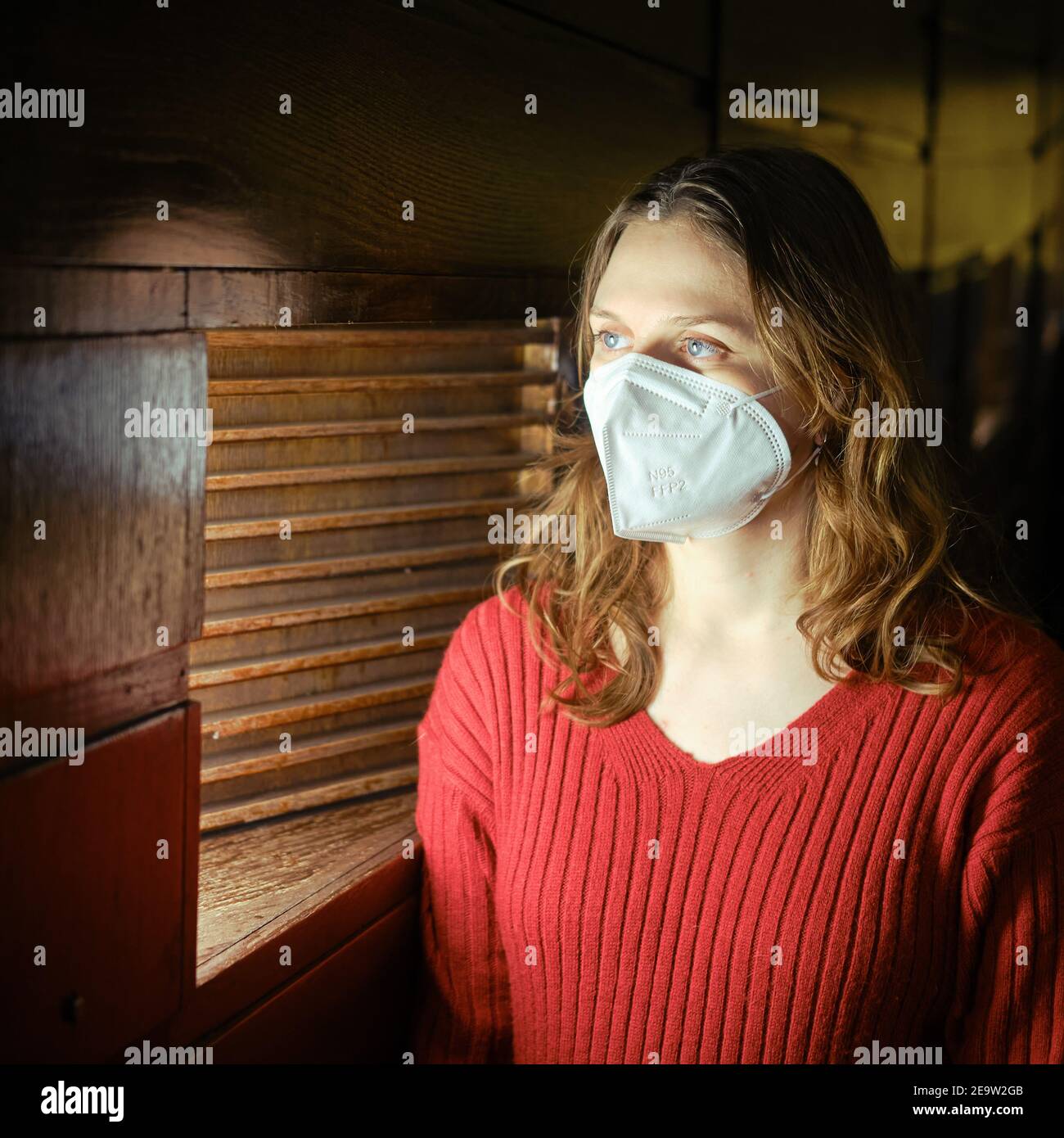 Young woman in medical mask ffp2 respirator looking out the ajar window ...