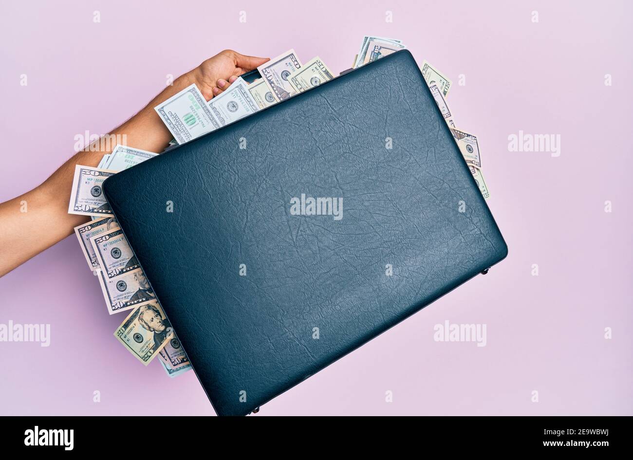 Hand of hispanic man holding briefcase with dollars over isolated pink ...