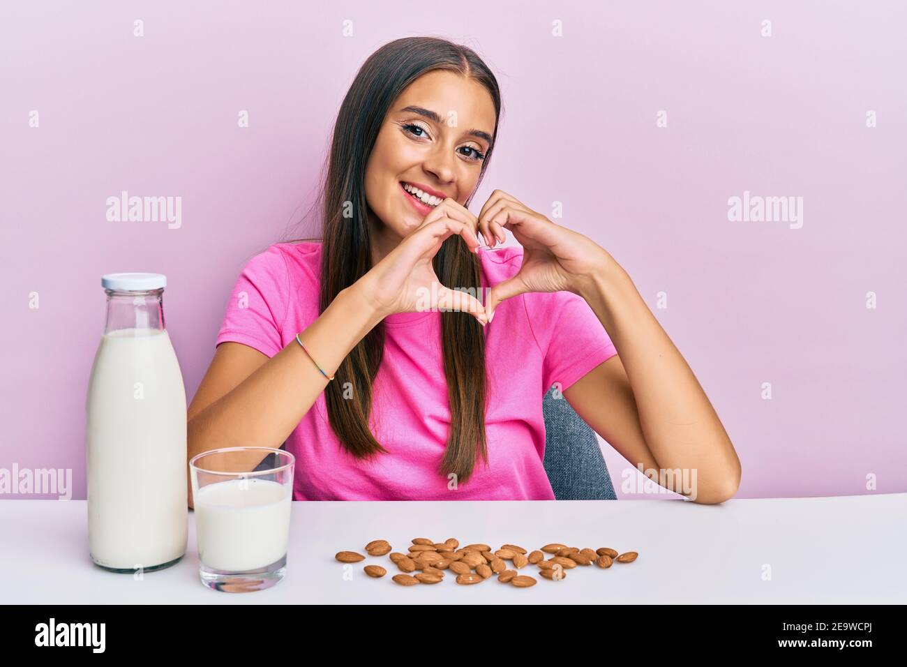 Young hispanic woman drinking healthy almond milk sitting on the table ...