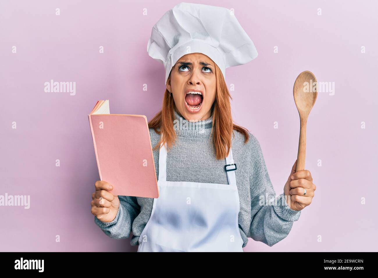 Hispanic young chef woman reading recipes book angry and mad screaming ...