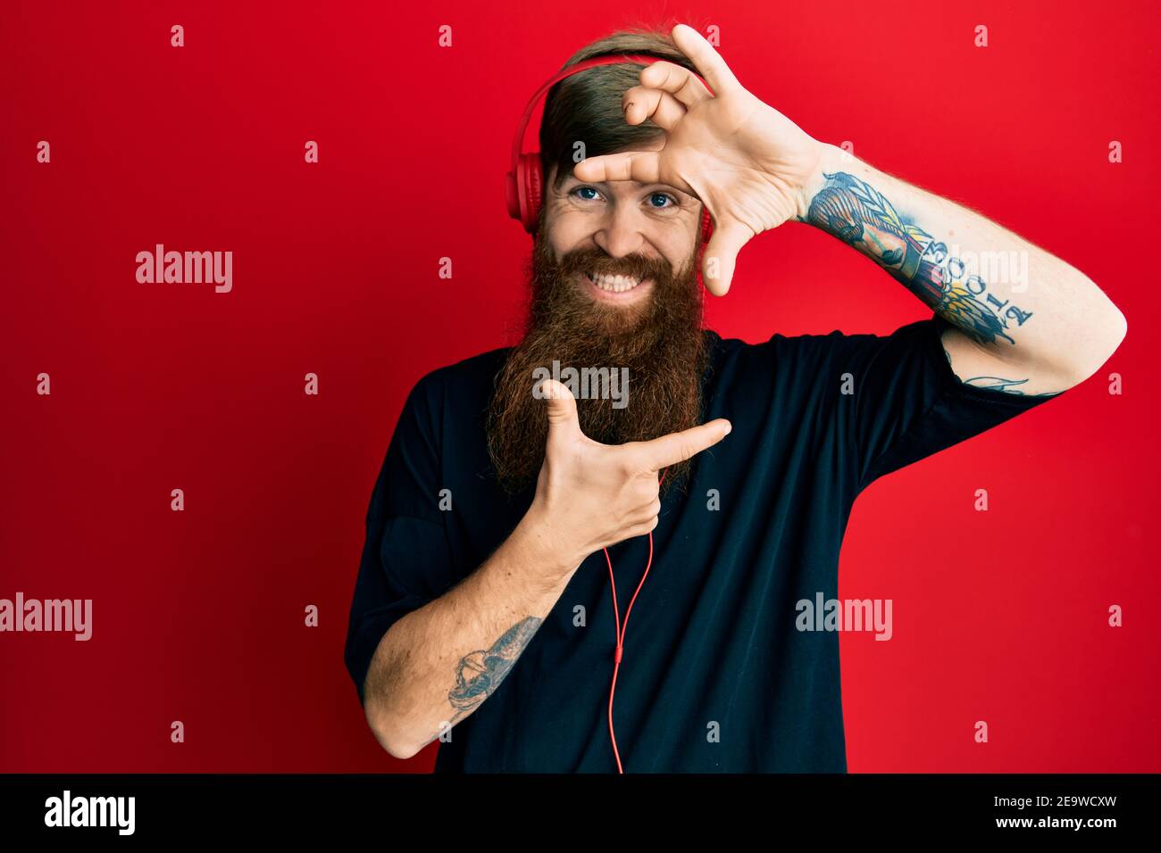 Redhead man with long beard listening to music using headphones smiling ...