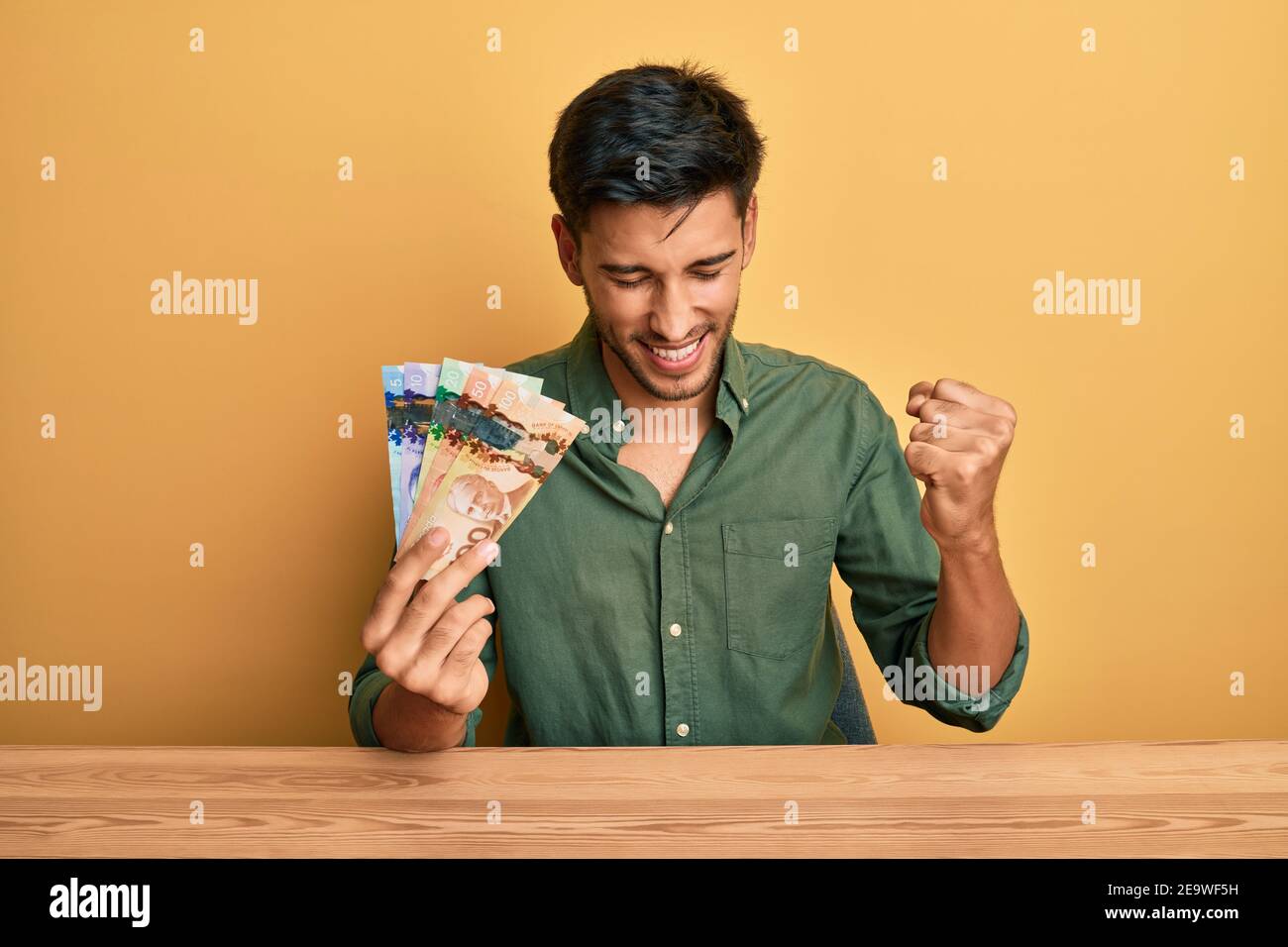Young handsome man holding canadian dollars very happy and excited ...