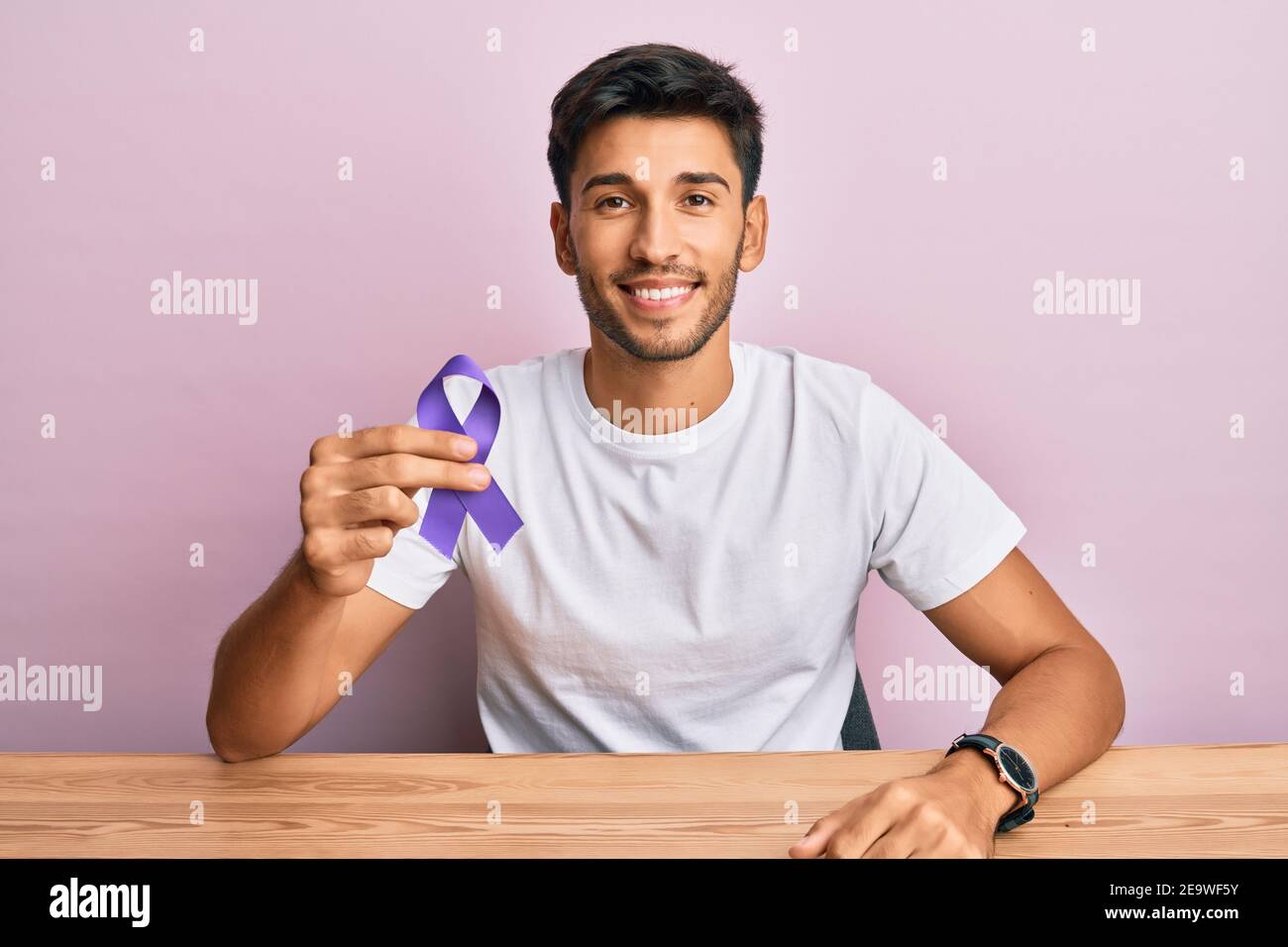 Young handsome man holding purple ribbon awareness looking positive and ...