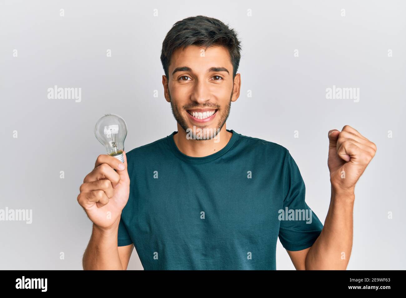 Young handsome man holding lightbulb for inspiration and idea screaming ...