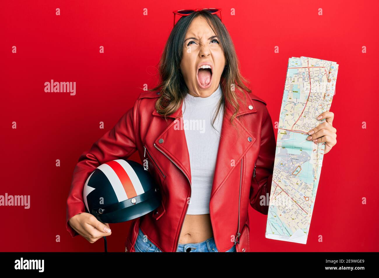 Young brunette woman holding motorcycle helmet and city map angry and ...