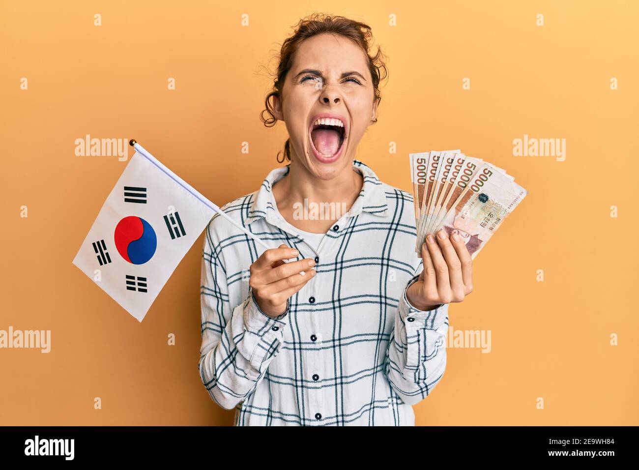 Young brunette woman holding south korean won banknotes angry and mad ...
