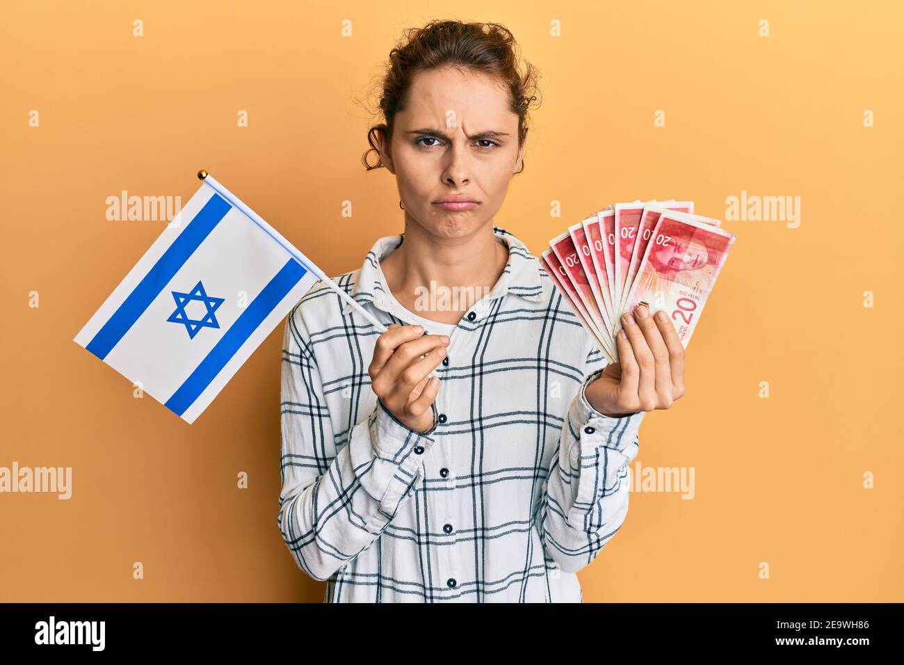 Young brunette woman holding israel flag and shekels banknotes ...