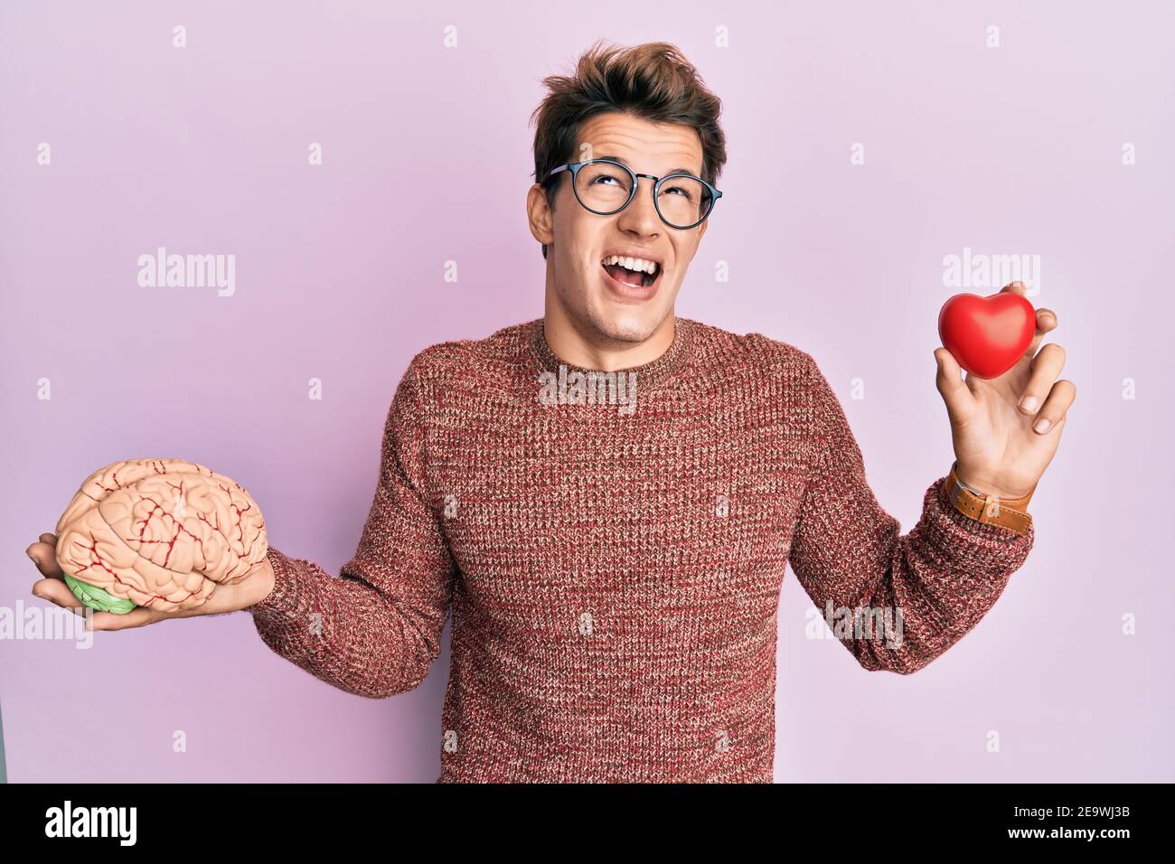 Handsome caucasian man holding brain and heart angry and mad screaming ...