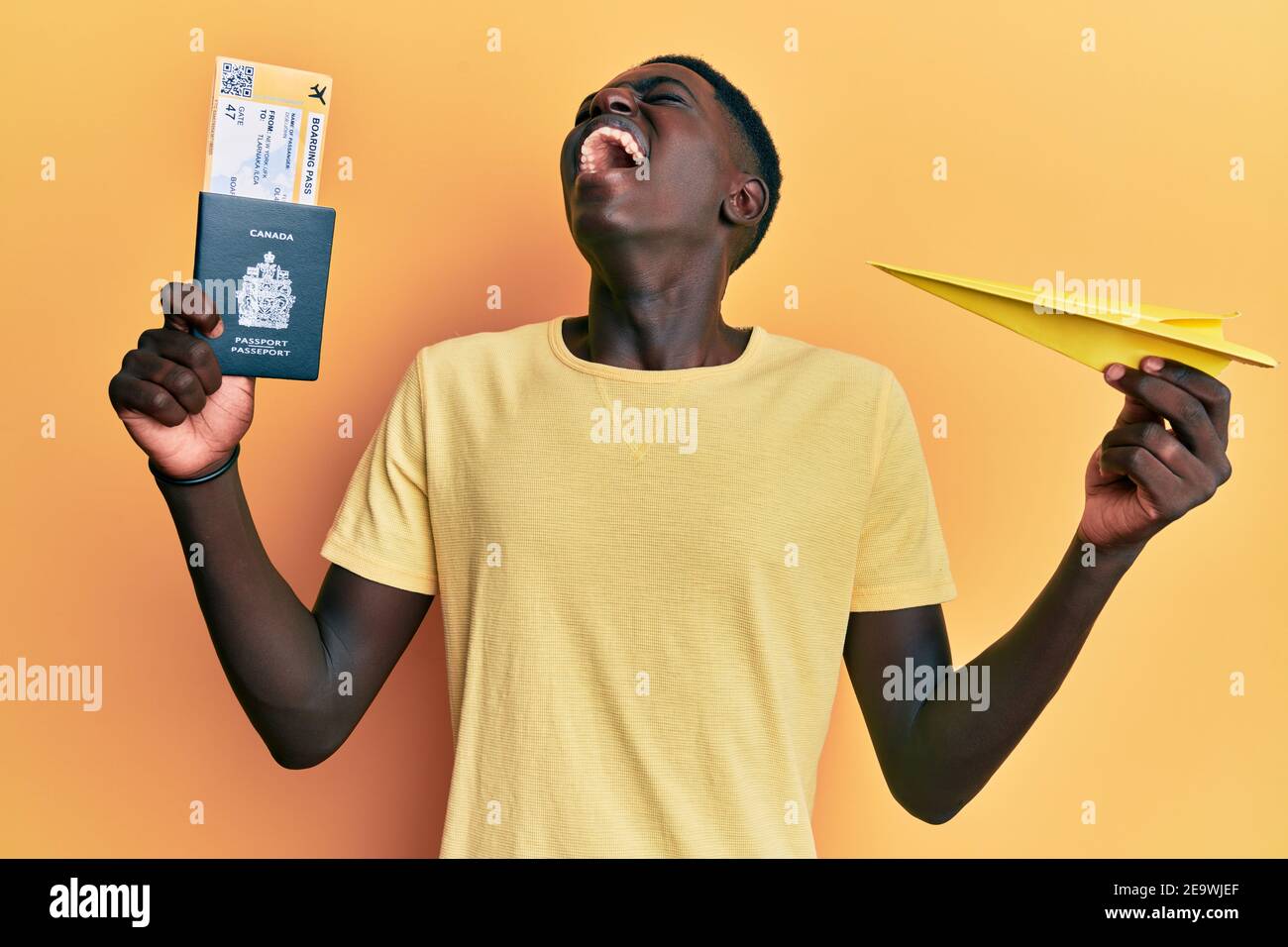 Young african american man holding paper plane and passport angry and ...