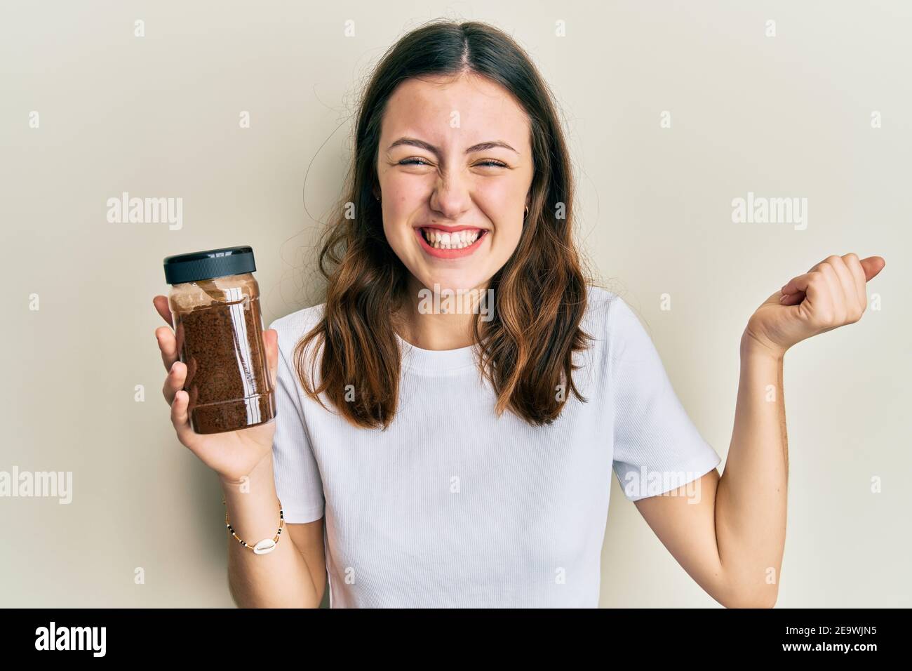 Young brunette woman holding soluble coffee screaming proud ...