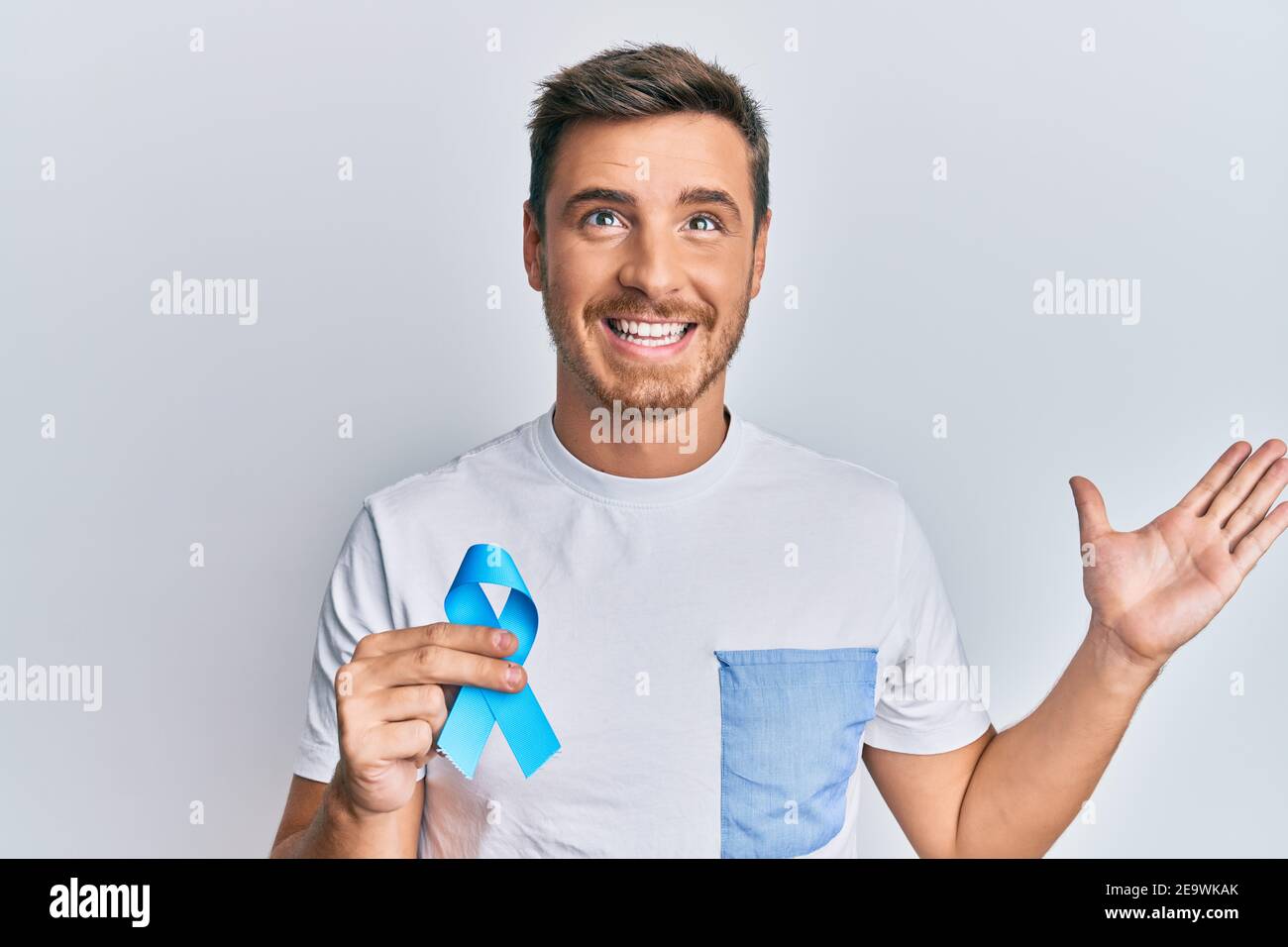 Handsome caucasian man holding blue ribbon celebrating victory with ...