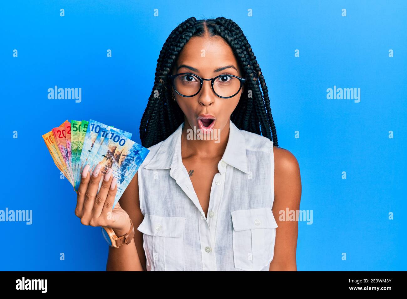 Beautiful hispanic woman holding swiss franc banknotes scared and ...